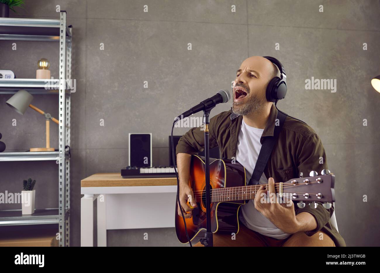 Male musician playing acoustic guitar and singing into microphone in ...