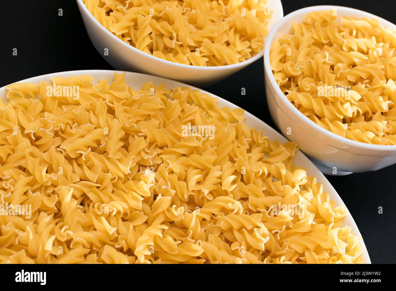 Uncooked Fusilli Pasta Lying on White Plate on Black Background. Raw ...