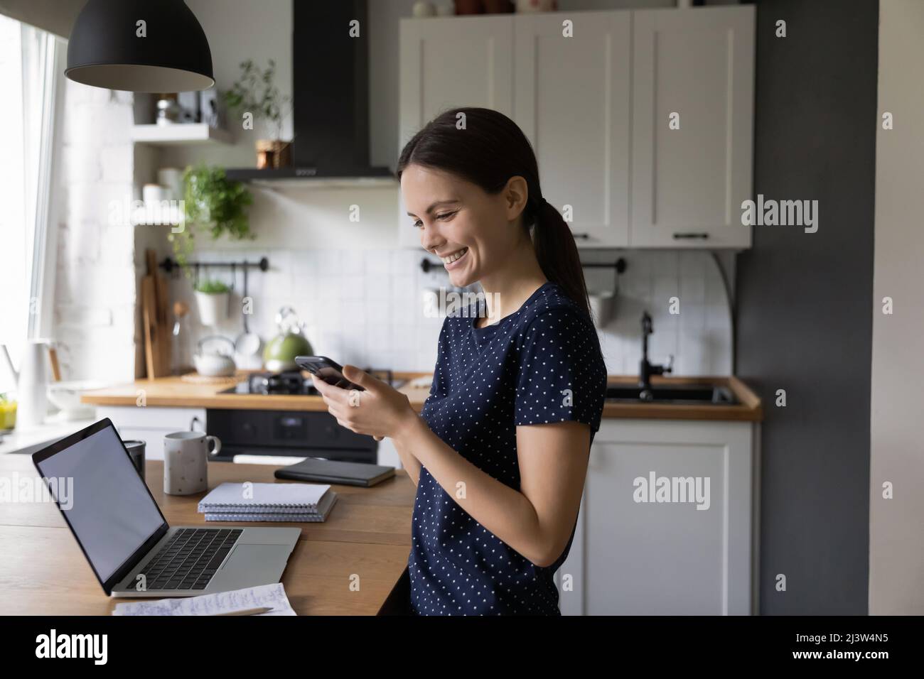 Woman holding smartphone standing near laptop white mockup on screen ...