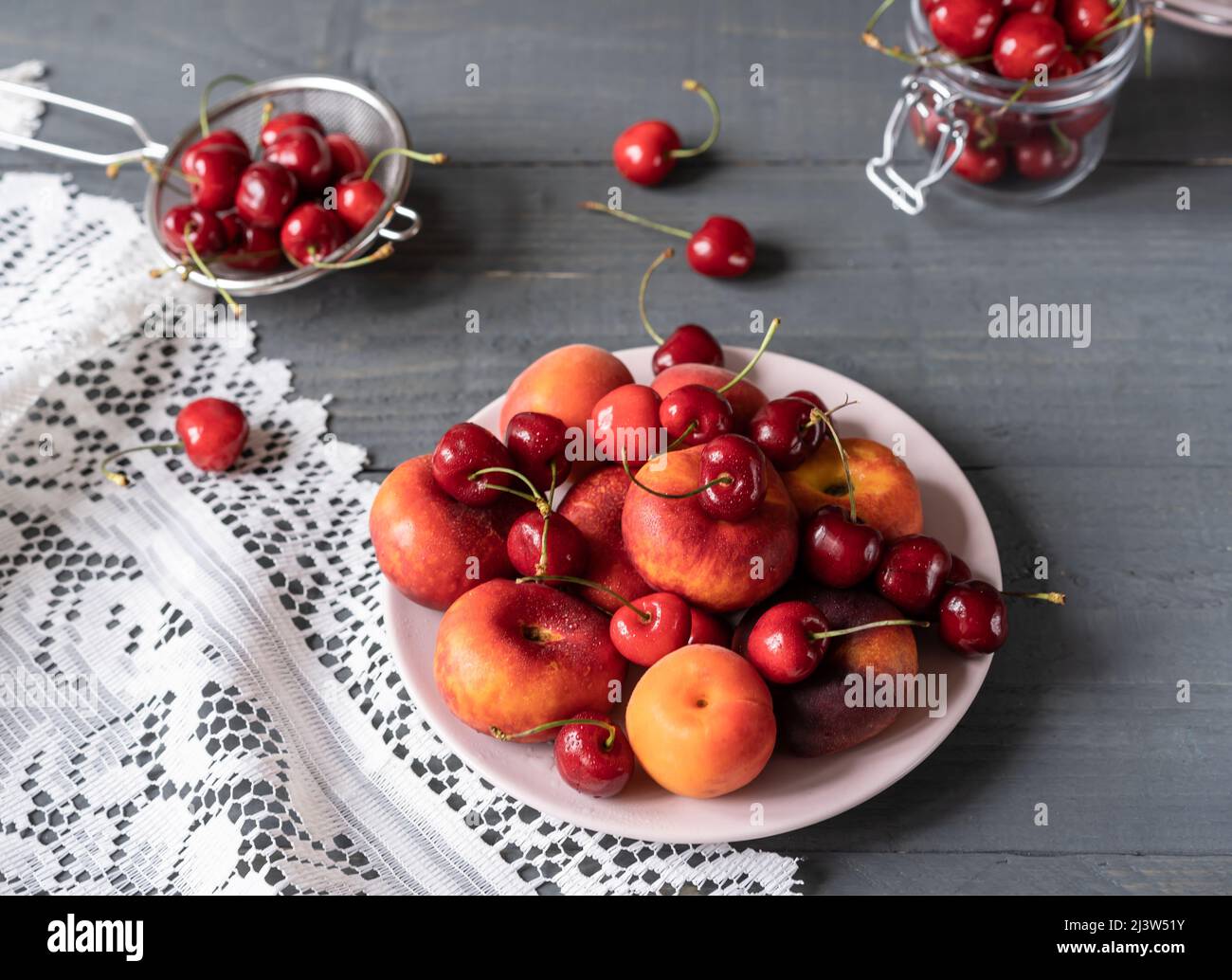 Fresh sweet cherries on plate and jar on white wooden table with blue ...