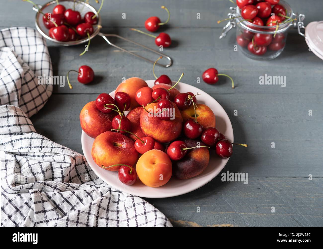 Fresh sweet cherries on plate and jar on white wooden table with blue ...
