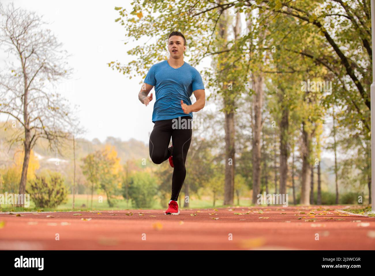 Attractive and handsome strong guy is running on the red track alone ...