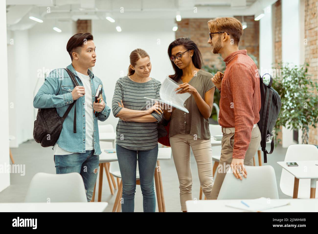 Four students standing and talking in classroom Stock Photo - Alamy
