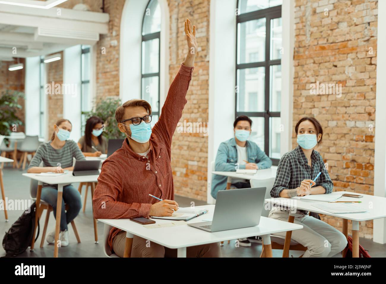 Male student in facial mask raising hand for answer Stock Photo - Alamy