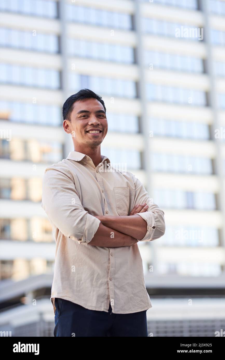 A young attractive Asian man stands in front of city buildings with ...