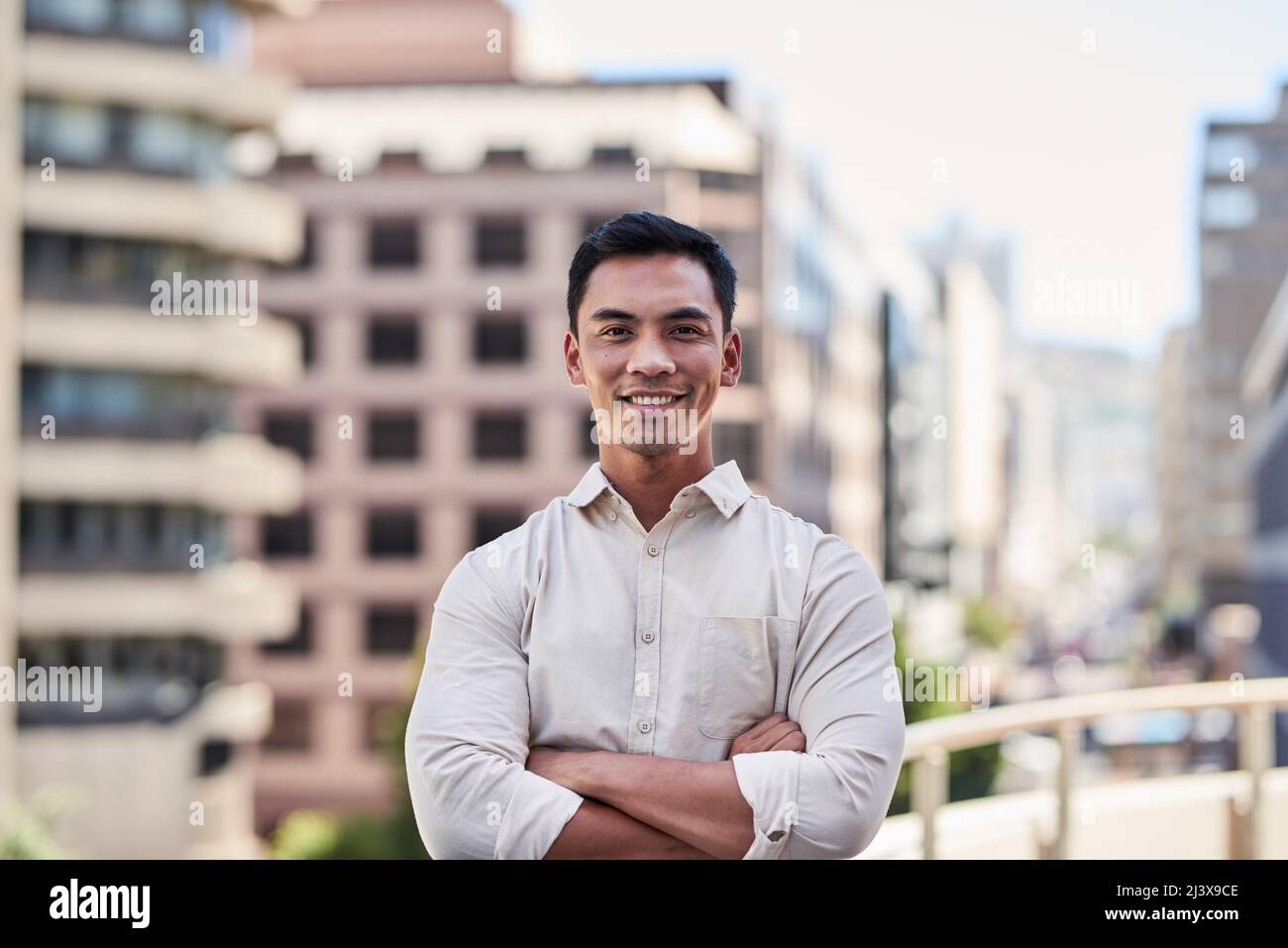 A young attractive Asian man stands in front of city buildings with ...