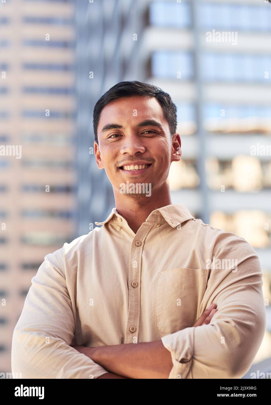 A young attractive Asian man smiles for portrait in front of city ...