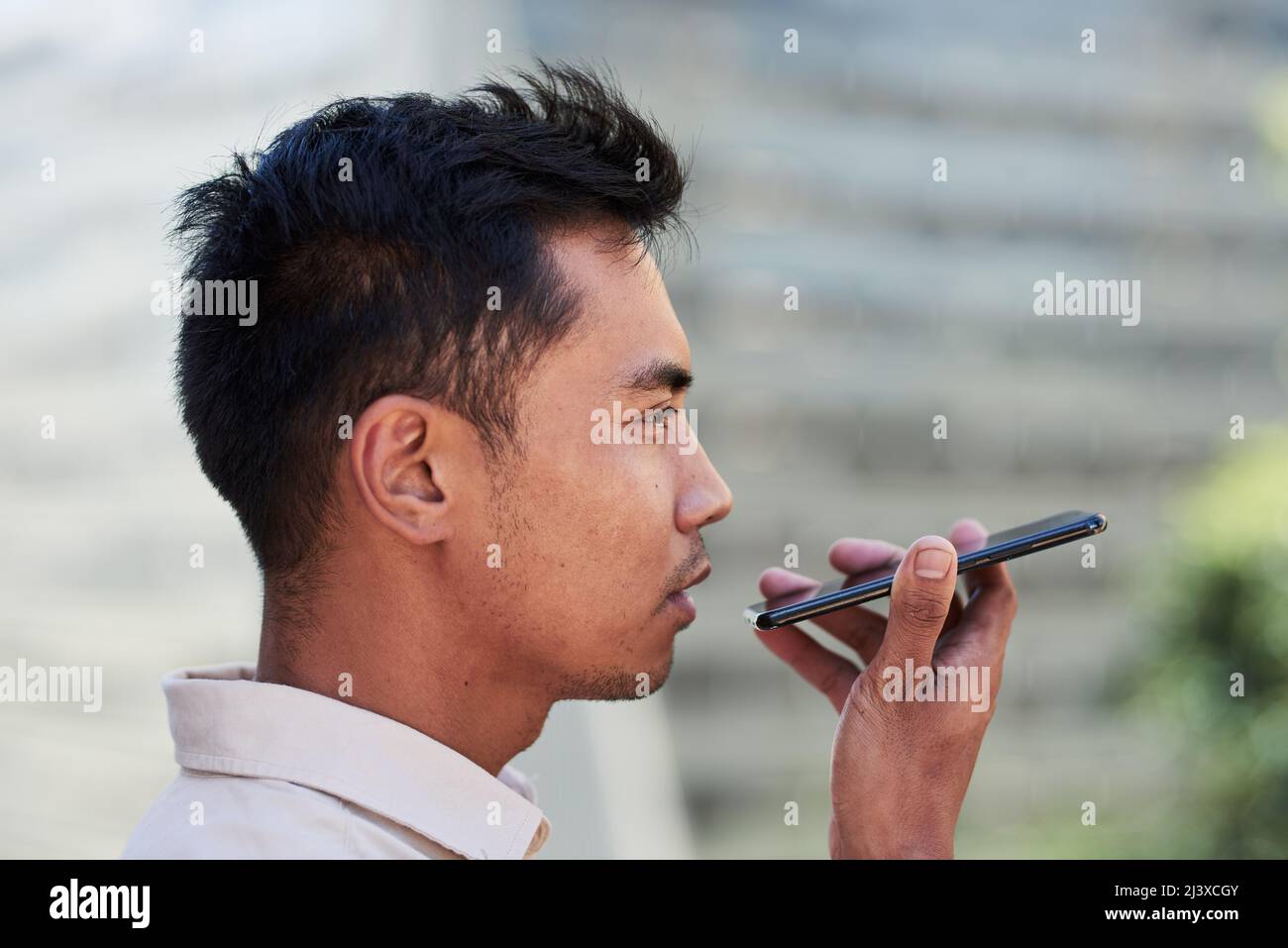 A young Asian man sends a voicenote using cellphone with city in ...