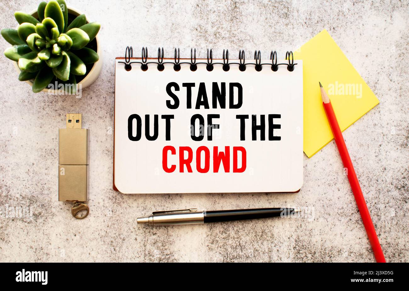 The words Stand out of the crowd written on a white notebook. Closeup ...