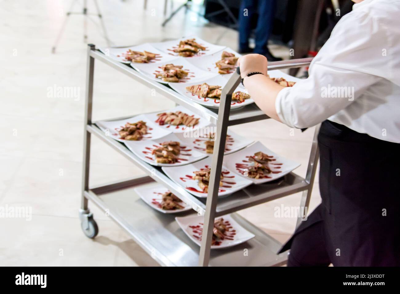 The waiter drives a cart with a meat dish Stock Photo - Alamy