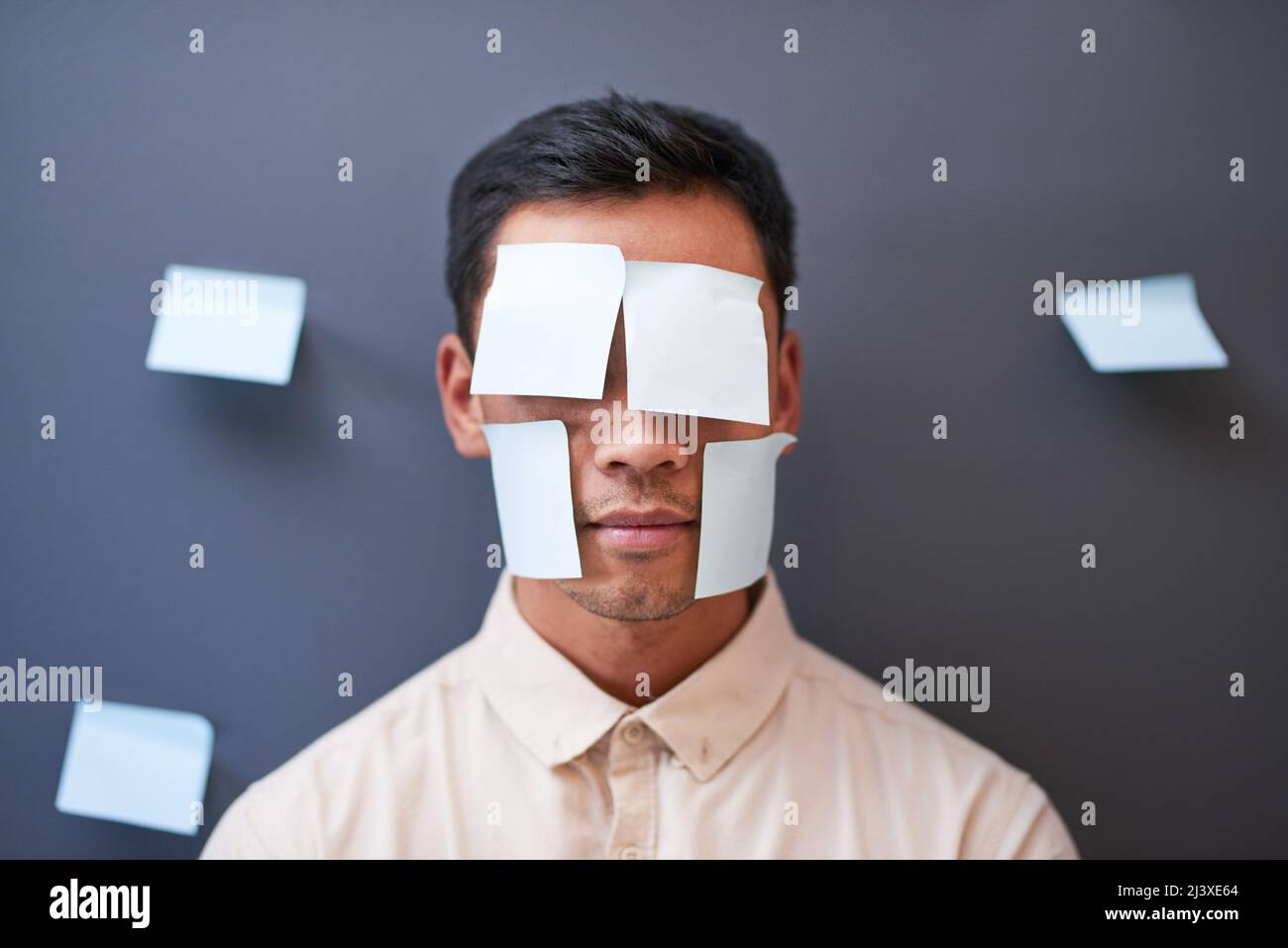 An Asian businessman stands with sticky notes on his face looking tired ...