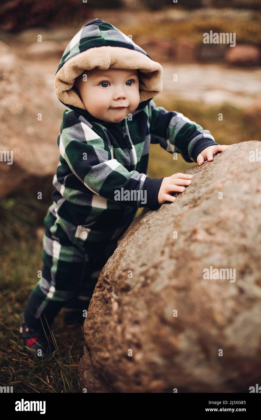 Adorable baby in warm overall with hood sitting on foliage Stock Photo ...