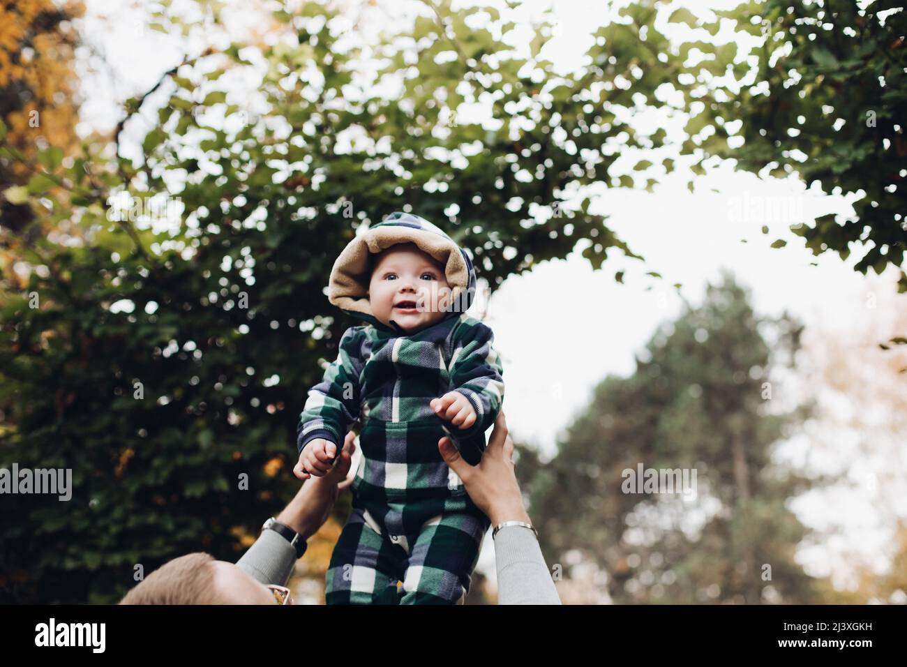 Adorable baby in warm overall with hood sitting on foliage Stock Photo ...