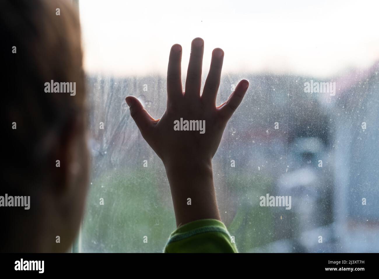 Young girl at window hands pressed against window, pensive or wanting ...
