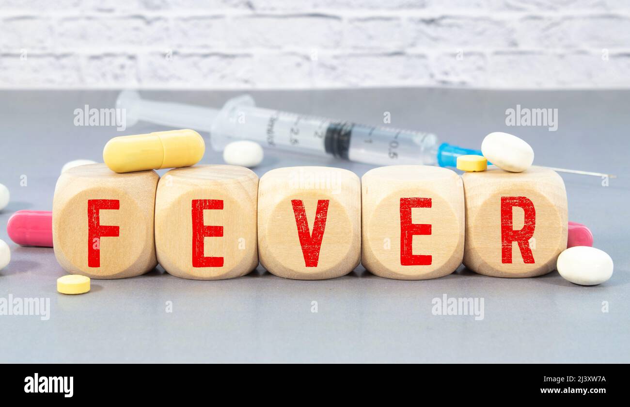 Wooden block form the word FEVER with stethoscope, pills, notepad, pen ...