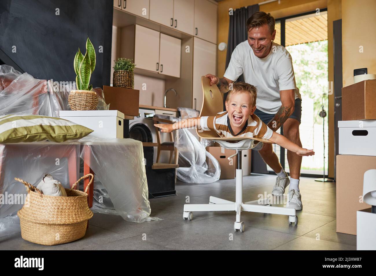 Portrait of carefree father playing with son riding on chair in hall ...