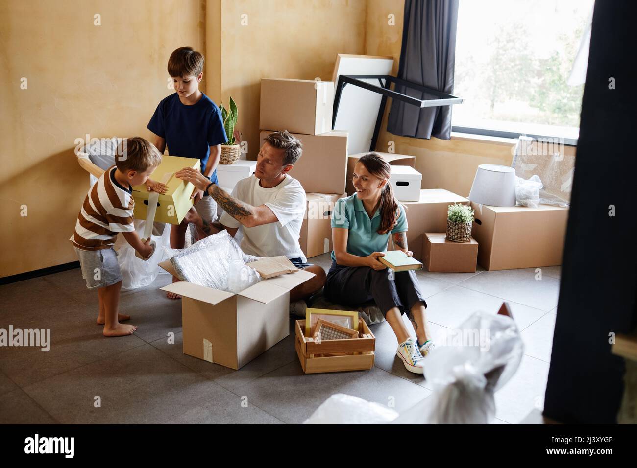 Full length portrait of happy family with two children unpacking boxes ...