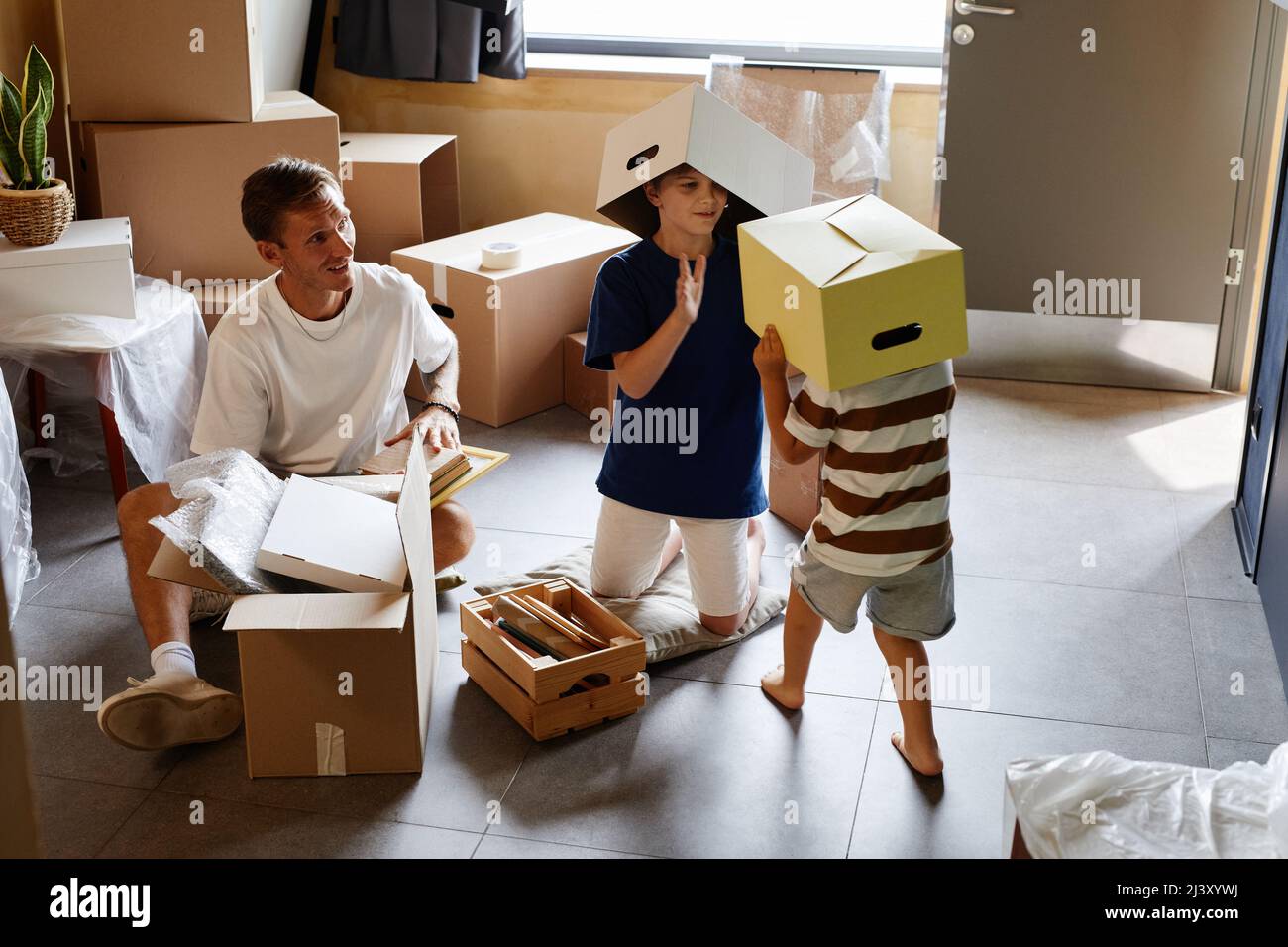 Portrait of two children playing with cardboard boxes while family ...