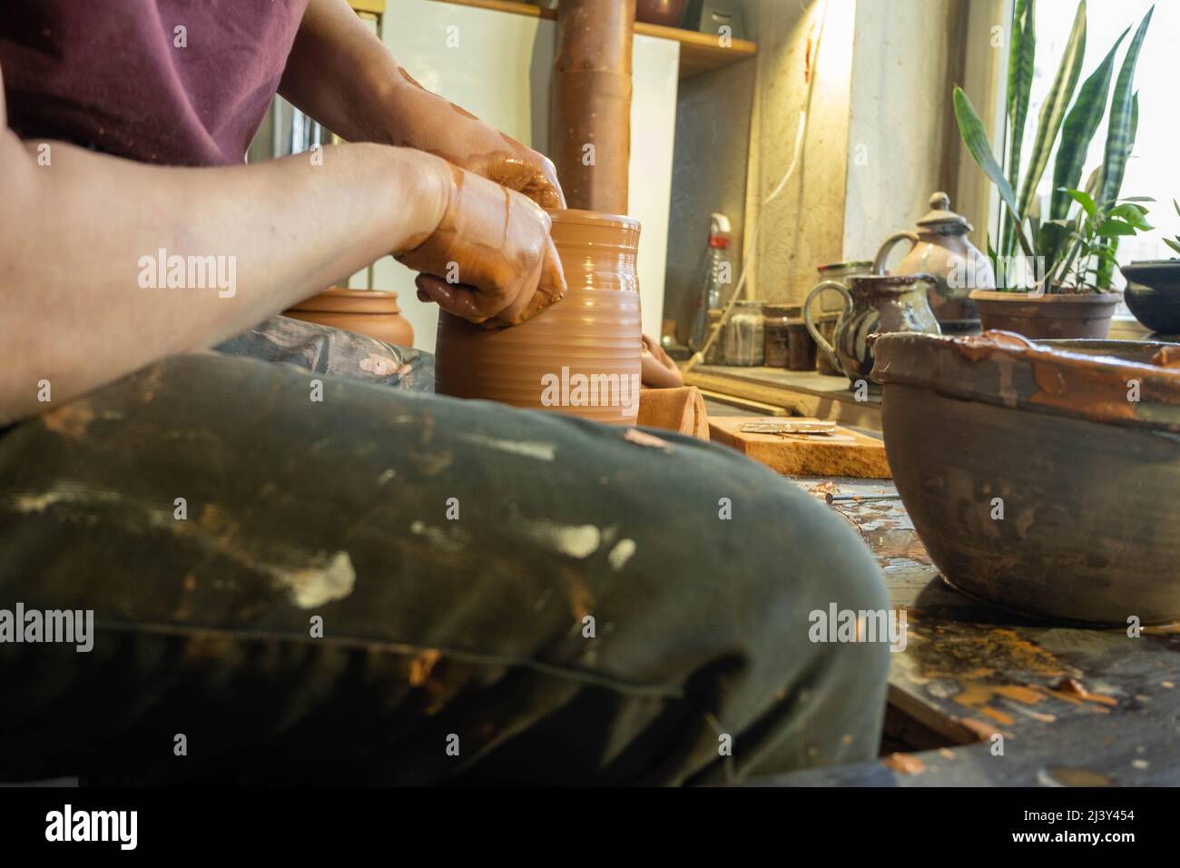 A master potter in an old craft workshop professionally forms a pot of ...