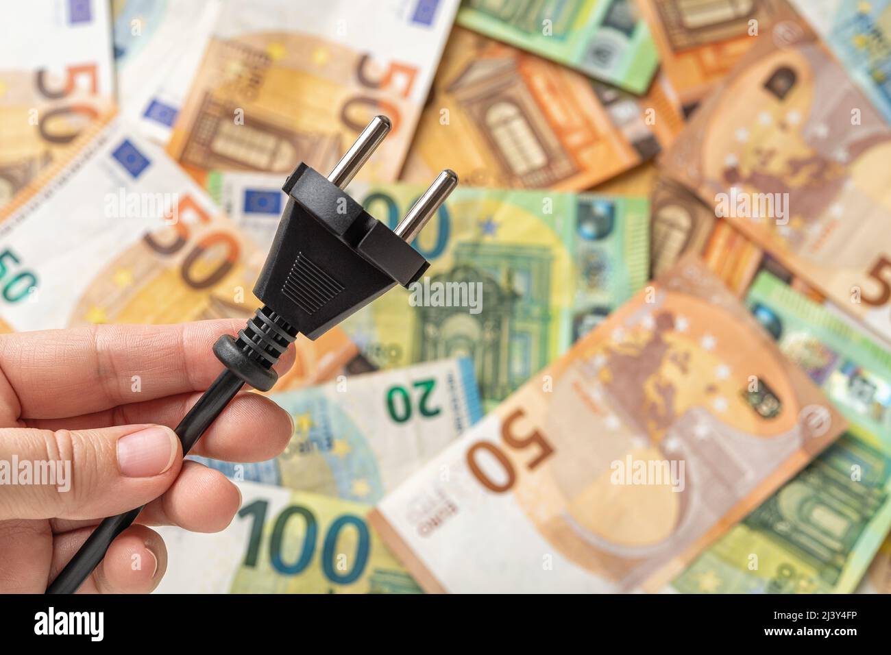 Woman hand holding black power plug over euro banknotes background ...