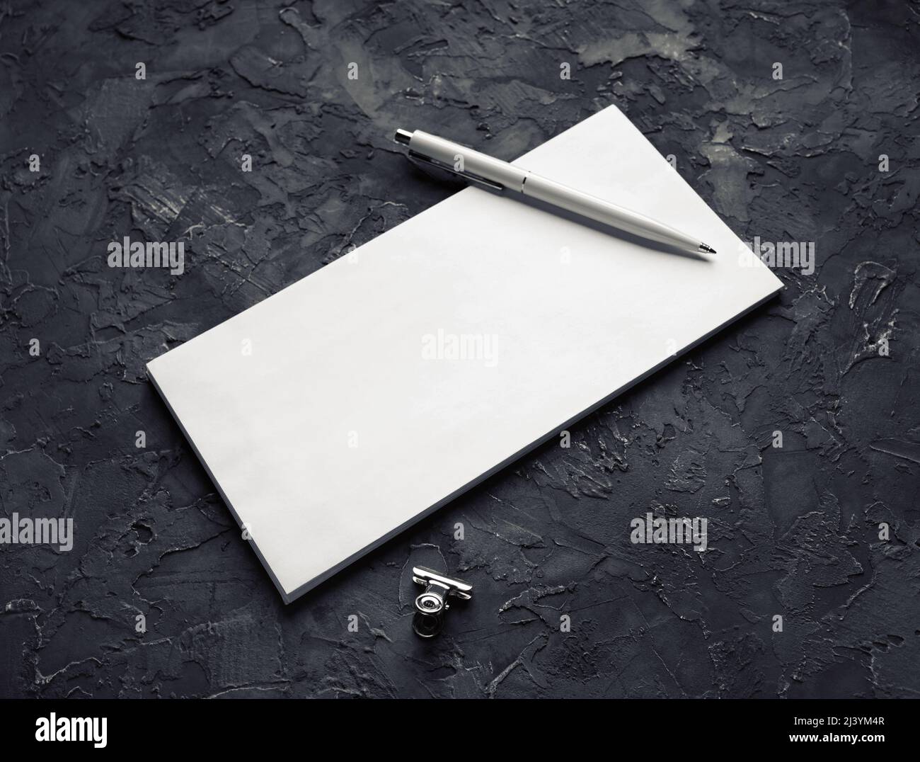 Photo of blank paper envelope, pen and metal clip on black plaster ...