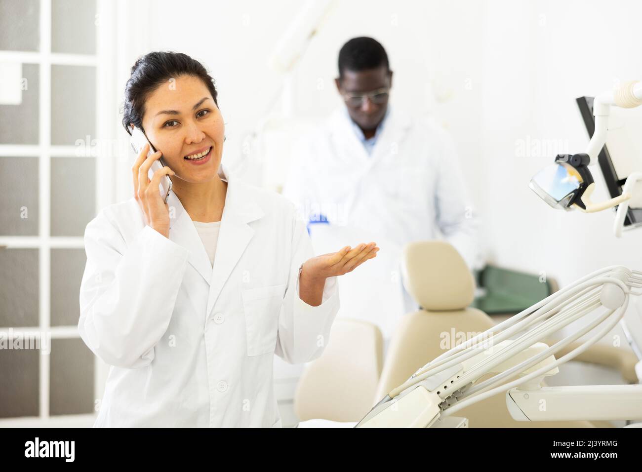 Portrait of friendly female dentist with a mobile phone. Invites ...