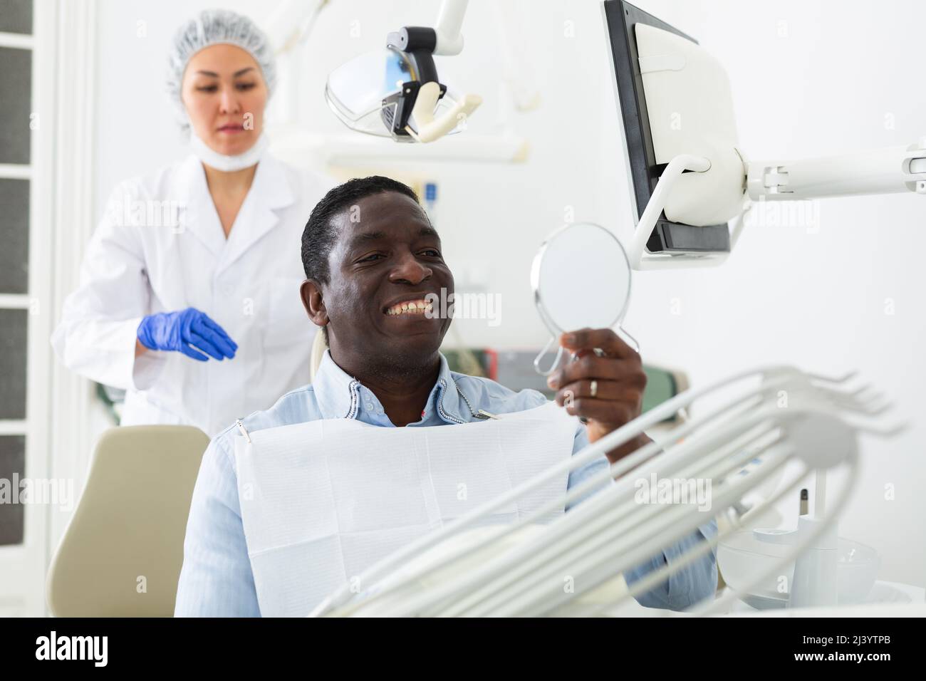 Man looking in mirror to evaluate results of dental restoration ...