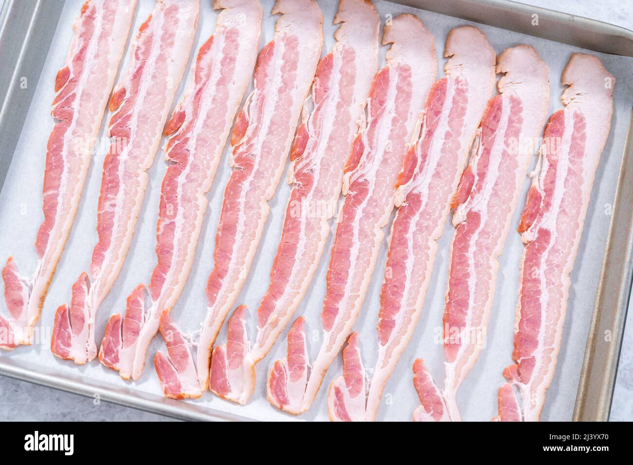 Uncooked bacon strips on a baking sheet with white parchment paper ...