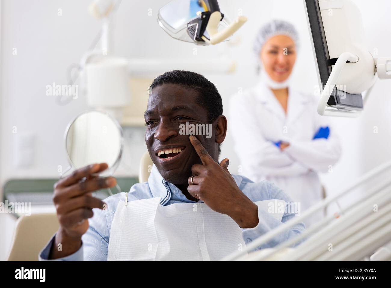 Man looking in mirror to evaluate results of dental restoration ...