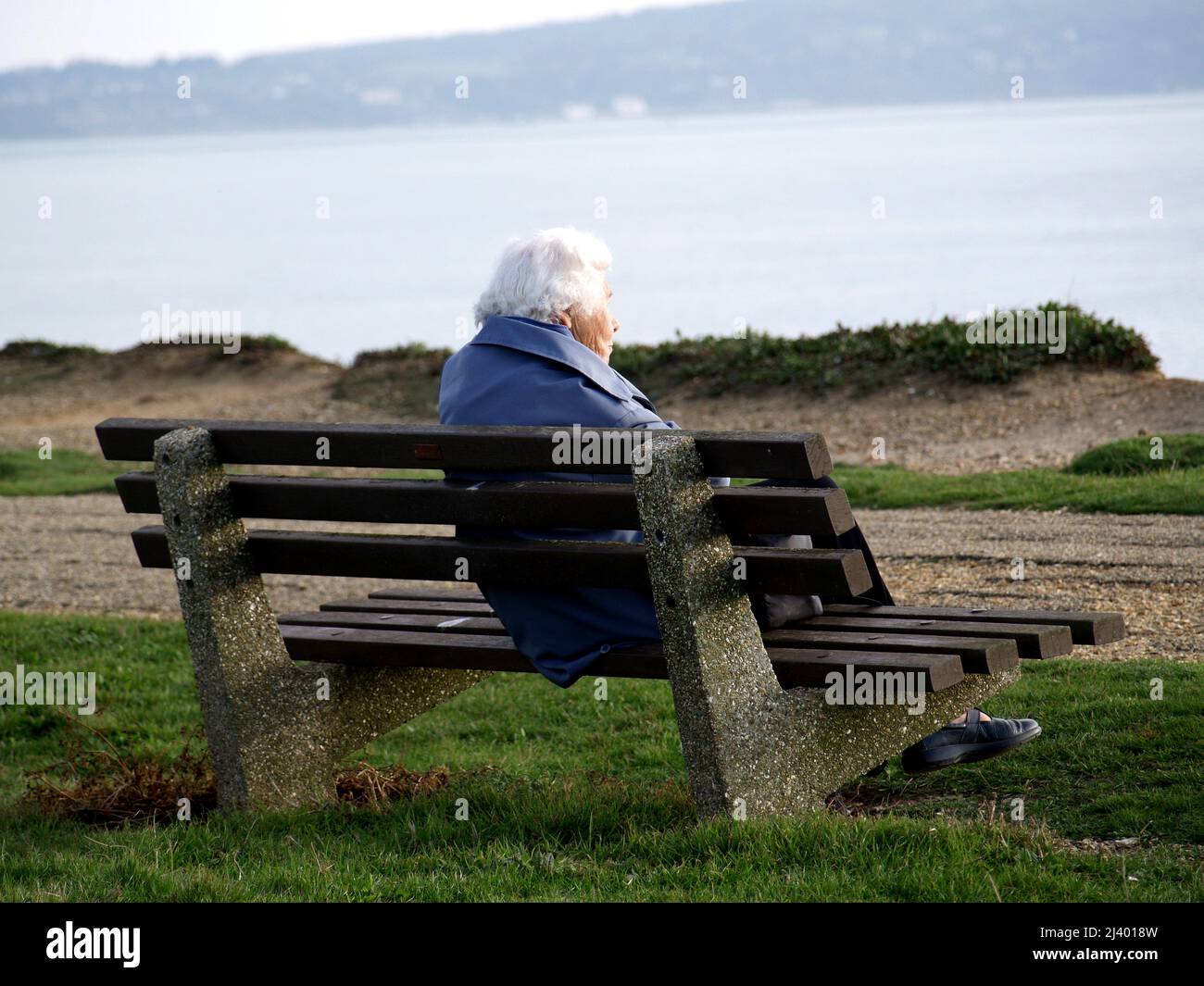 Elderly person sat on bench overlooking the sea at New Milton ...
