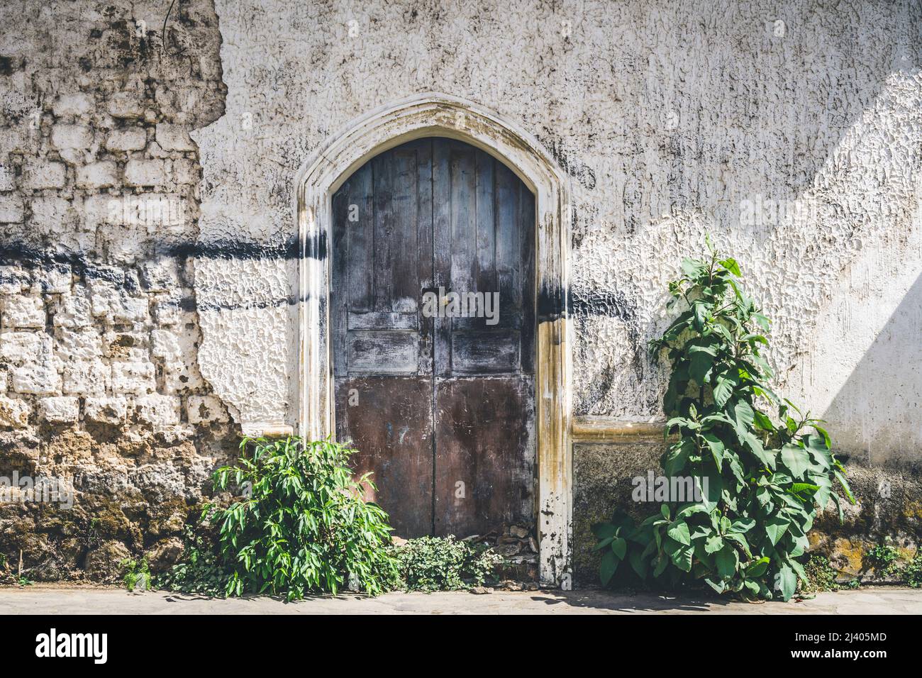 Old house with arched wooden door and crumbling wall exposing brick ...