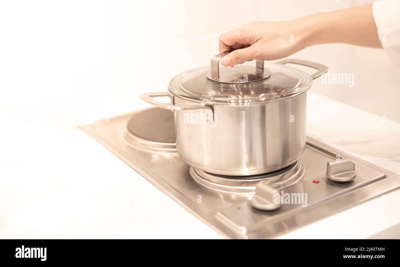 Female hand holding a pot that is put on the electric pan in the ...