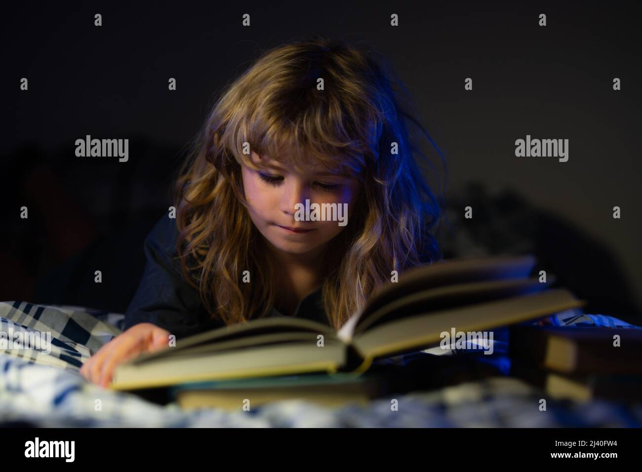 Child reading a book in bed before going to sleep. Little boy lying on ...