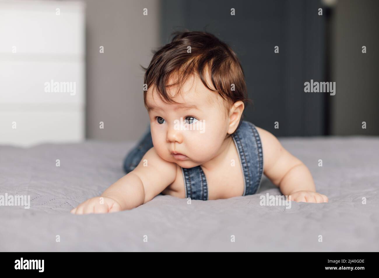Portrait of pretty baby wearing denim romper lying on gray blanket at ... Portrait of pretty baby wearing denim romper lying on gray blanket at ...