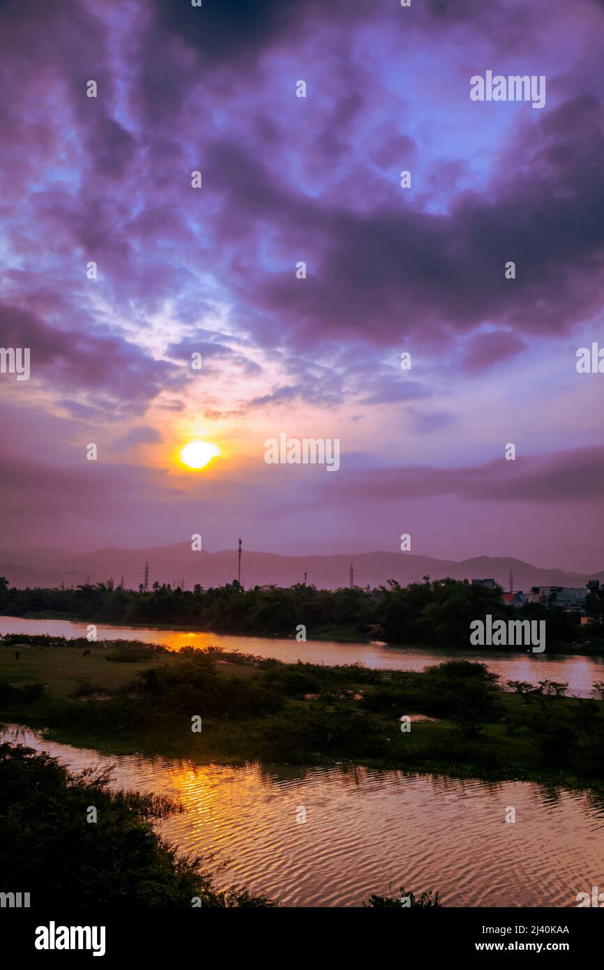 A yellow sun getting low in the sky among blue purple clouds Stock ...