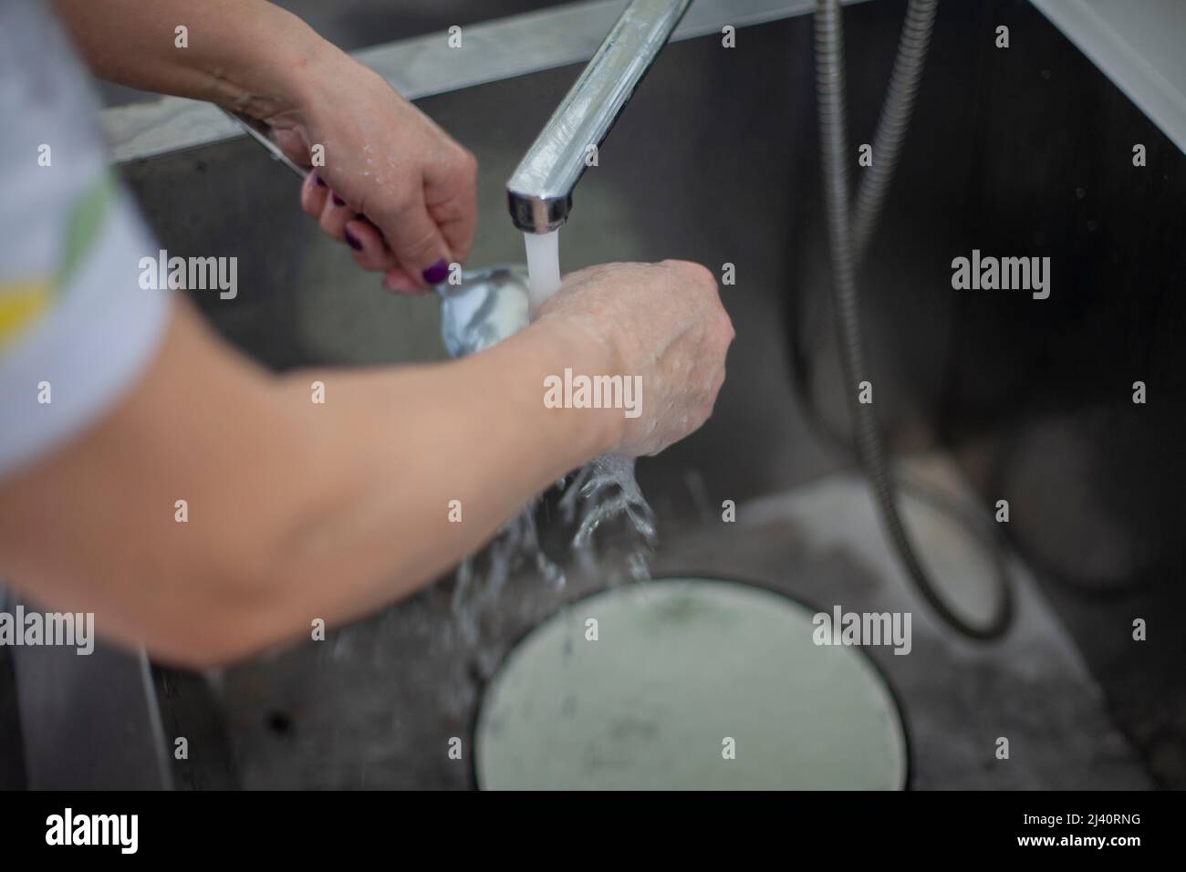 Woman washes dishes under stream of water. Kitchen details. Dishwasher ...