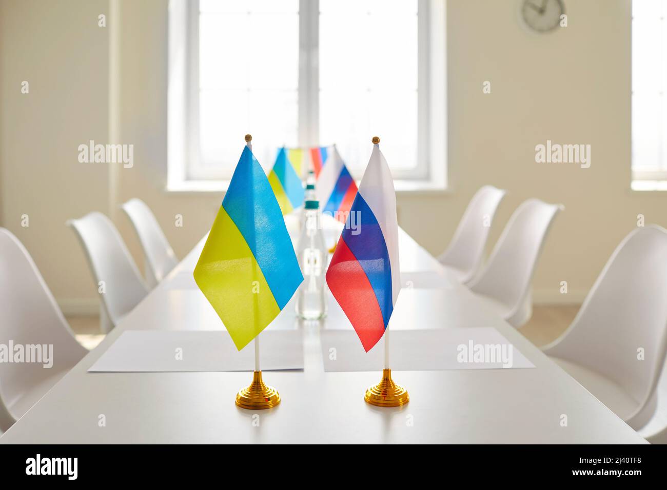 Ukrainian and Russian flags standing on long table with chairs in empty ...