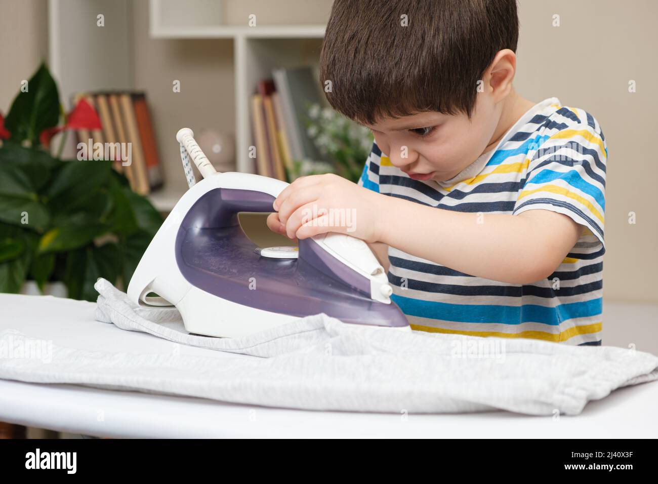 A boy of 4 years learns to hold an iron, iron clothes on an ironing ...