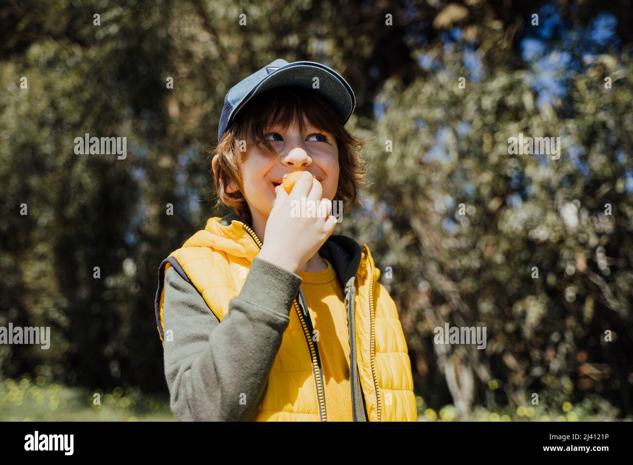 Smiling cheerful child kid in yellow vest and green hoodie eats crisp ...