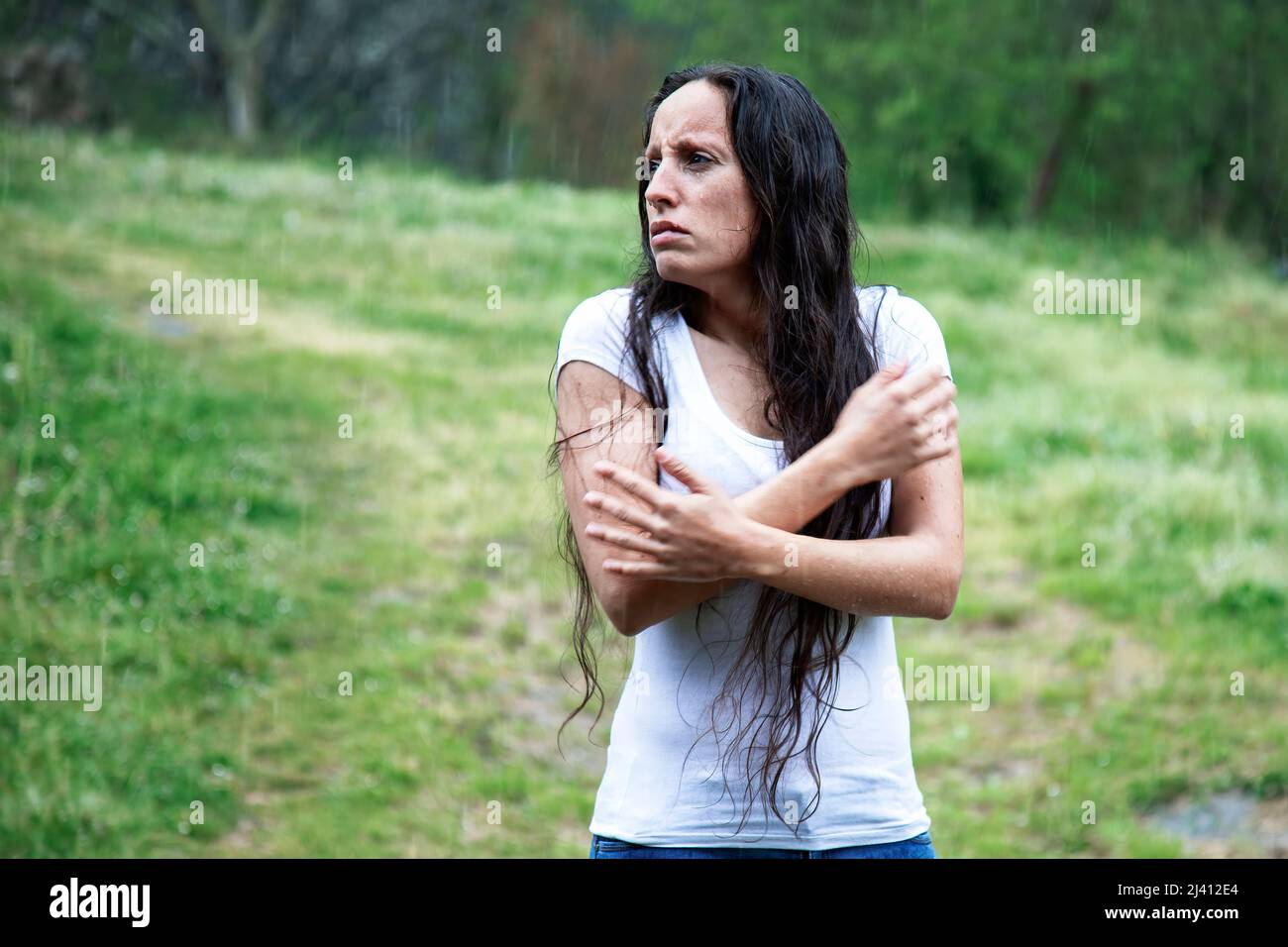 long-haired brunette girl in the rain hugging herself, feeling lonely ...
