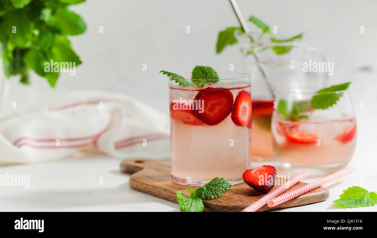 Homemade refreshing strawberry lemonade in glasses and jug with fresh strawberries and mint ...