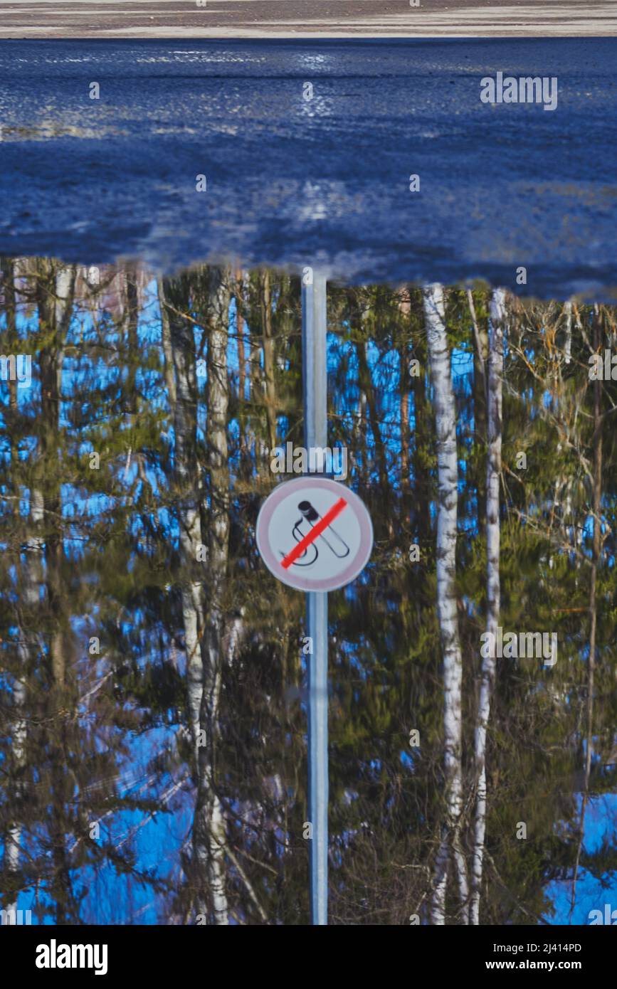 A blurry reflection in a puddle. A no smoking sign on a pole at a gas ...
