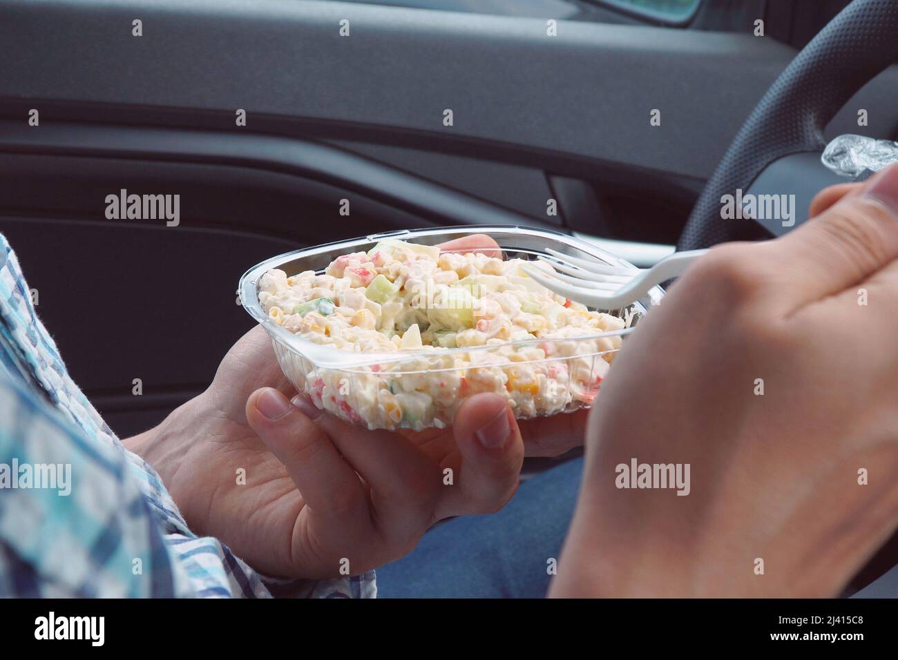 A man, sitting in a car, eats a salad with mayonnaise from plastic ...