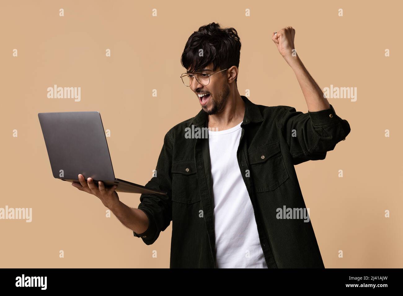 Lucky indian guy using laptop, raising hand up on beige Stock Photo - Alamy