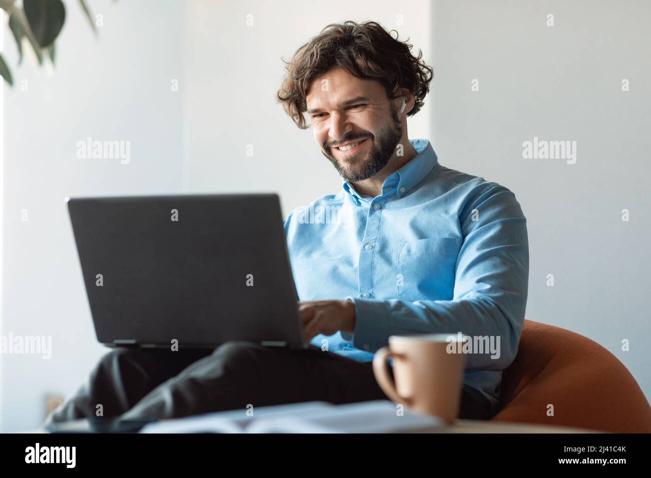 Smiling businessman using laptop sitting on beanbag in office Stock ...