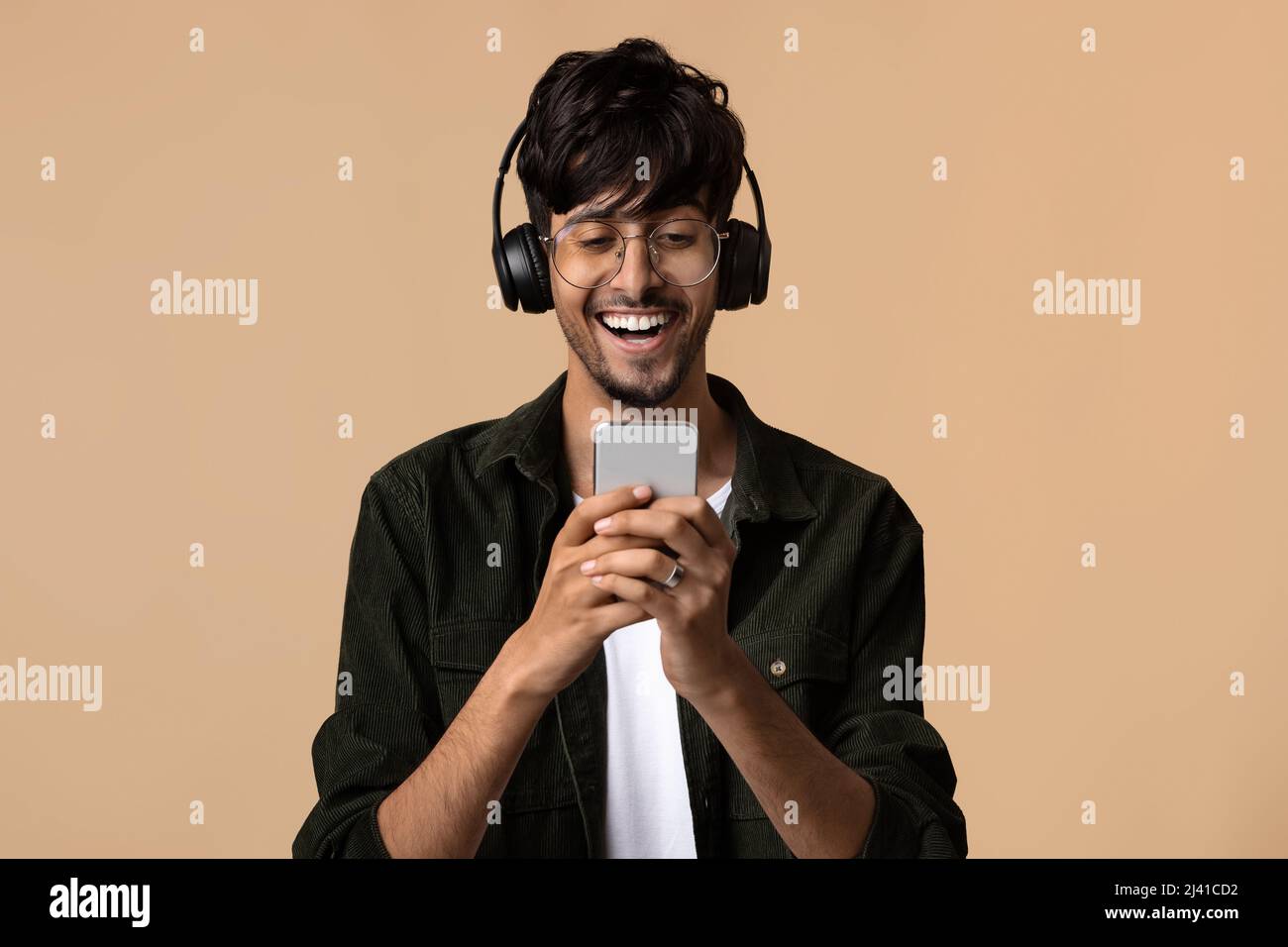 Cheerful indian guy watching videos on smartphone, using headset Stock ...