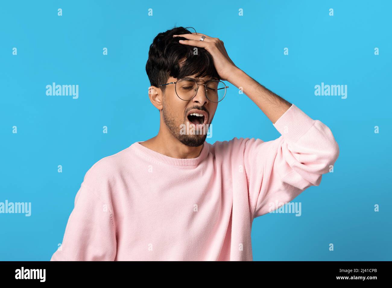 Overwhelmed indian guy touching his head, blue studio background Stock ...