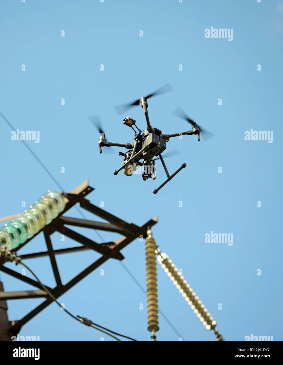 Pro quadcopter with camera aboard flying in a sky, electric pylon ...