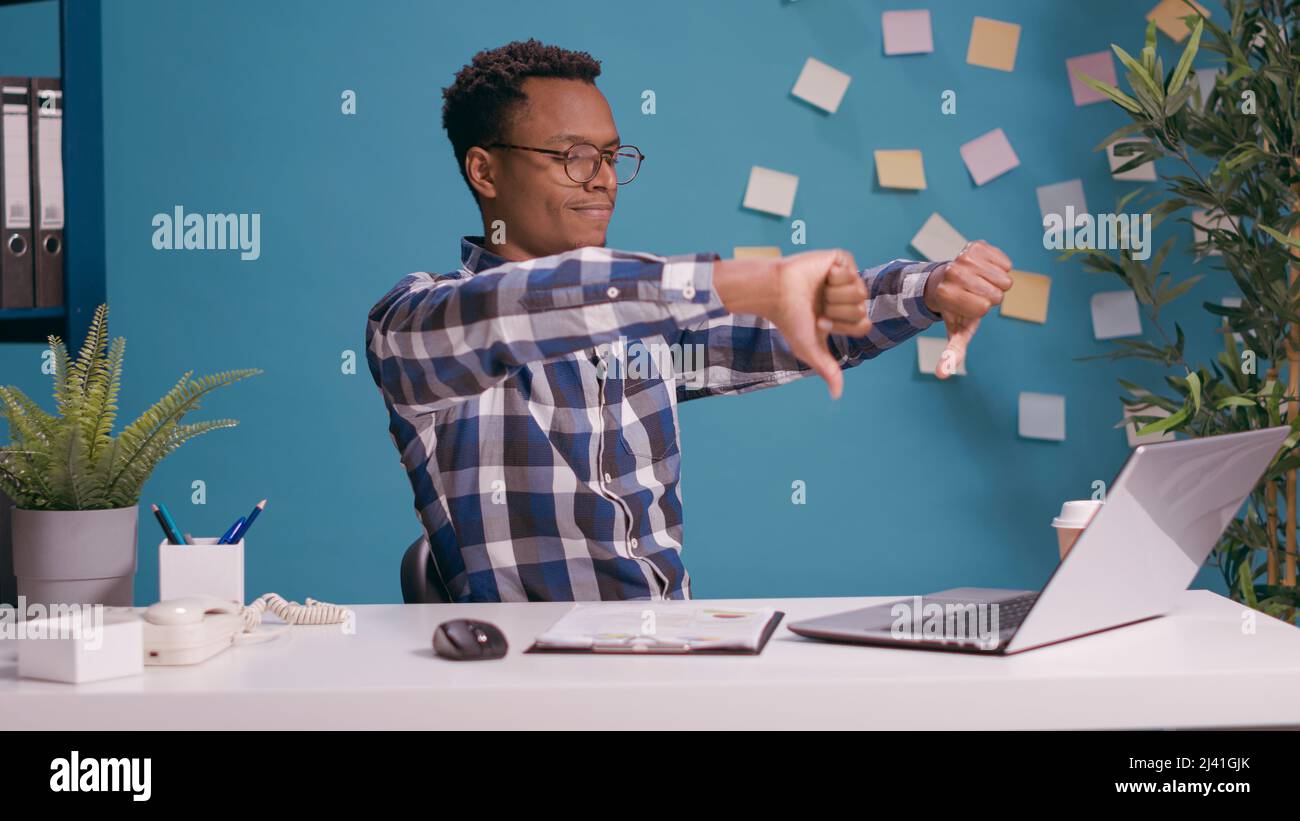 Office employee giving thumbs down in front of laptop screen, showing ...
