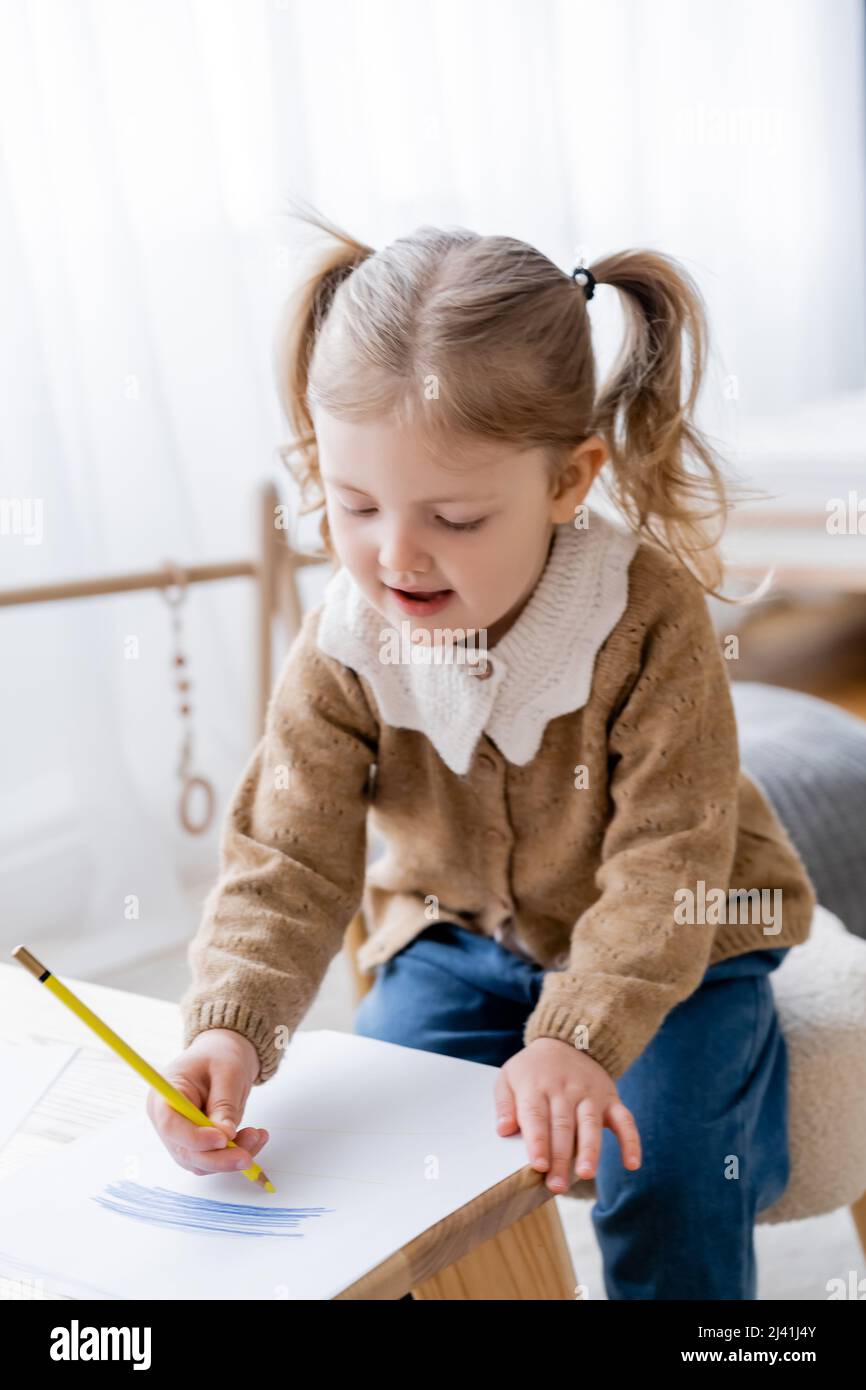 concentrated girl drawing with yellow pencil on paper with blue strokes ...